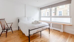 Quarto com cama, uma cadeira e uma janela grande.