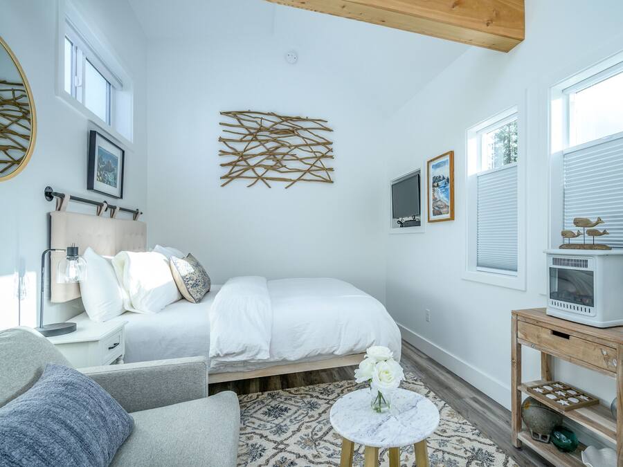 Um quarto moderno com cama, mesa de cabeceira, abajur e uma pequena mesa redonda com flores.