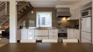 Uma cozinha moderna com armários brancos, uma mesa de jantar de madeira, forno embutido e micro-ondas.