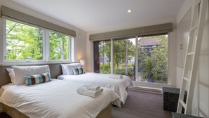 Quarto de hotel com duas camas, janelas amplas e vista para árvores e edifícios.