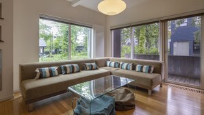 Uma sala de estar moderna com um sofá modular, uma mesa de centro de vidro e grandes janelas com vista para o exterior.