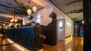 Uma área de recepção com design moderno, destacando-se por um balcão de madeira, uma parede de pedra e luminárias pendentes.
