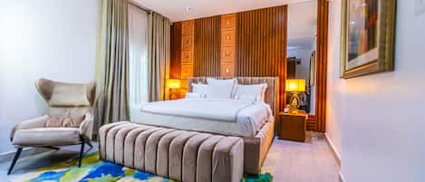 Quarto de hotel moderno com uma cama grande, uma poltrona, um tapete colorido e uma mesa de cabeceira com luminária.