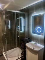 Um banheiro moderno com chuveiro em box de vidro, pia branca e espelho com iluminação circular.