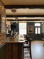 Uma área de bar com balcão de madeira, banquetas e uma janela grande com vitrais.