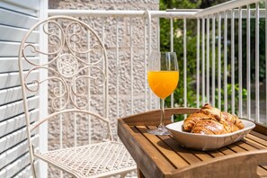 Uma mesa de madeira com um cesto de croissants e um copo de suco de laranja numa varanda.
