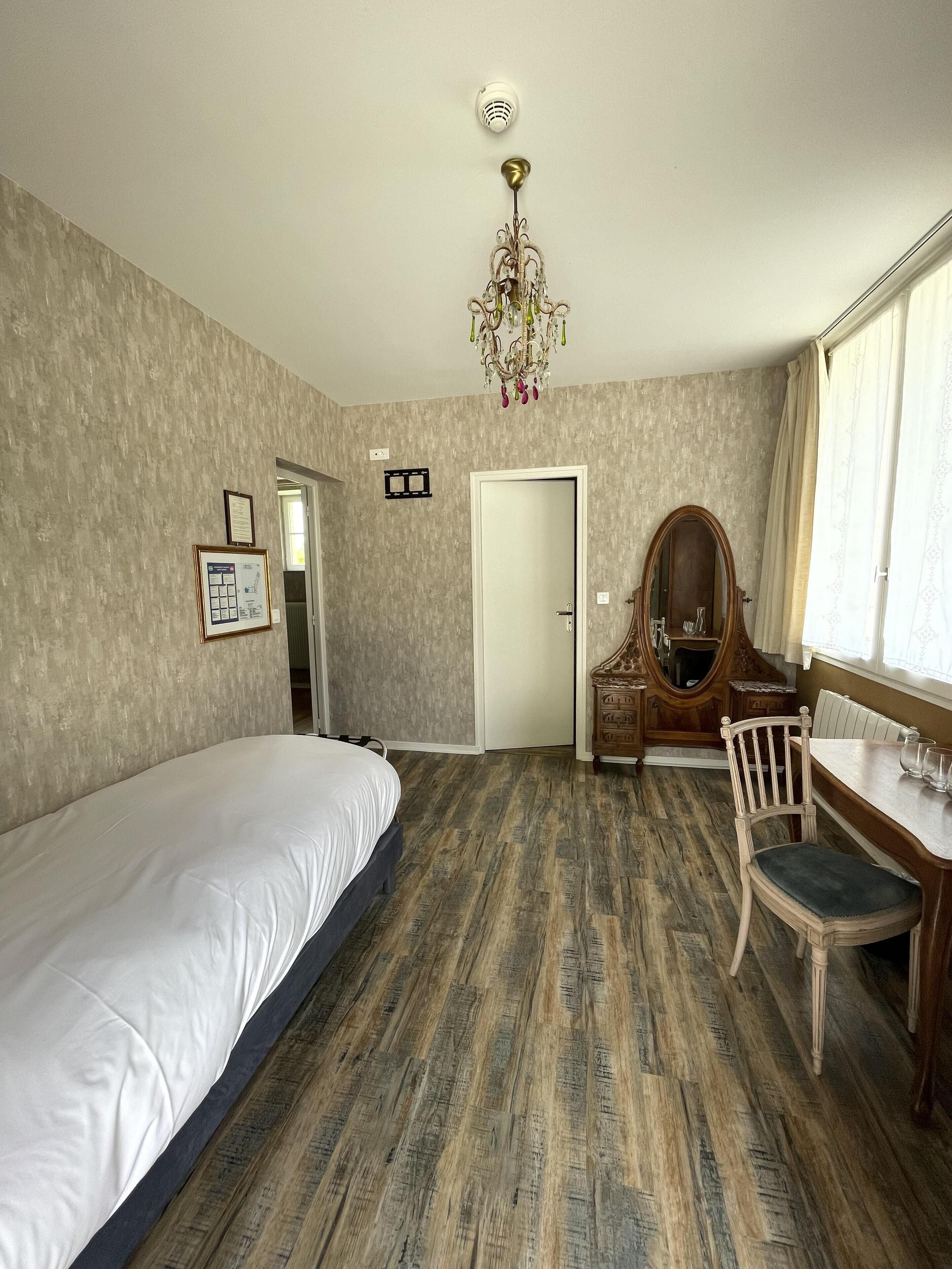 Quarto com cama, escrivaninha com cadeira, cômoda, espelho e lustre.