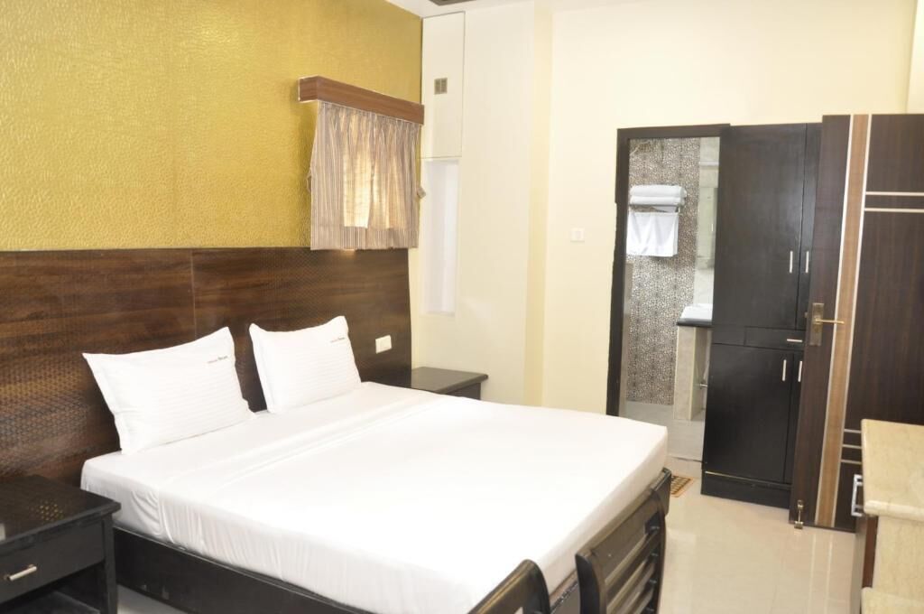 Quarto de hotel com cama, mesa de cabeceira, guarda-roupa e banheiro com chuveiro e vaso sanitário.