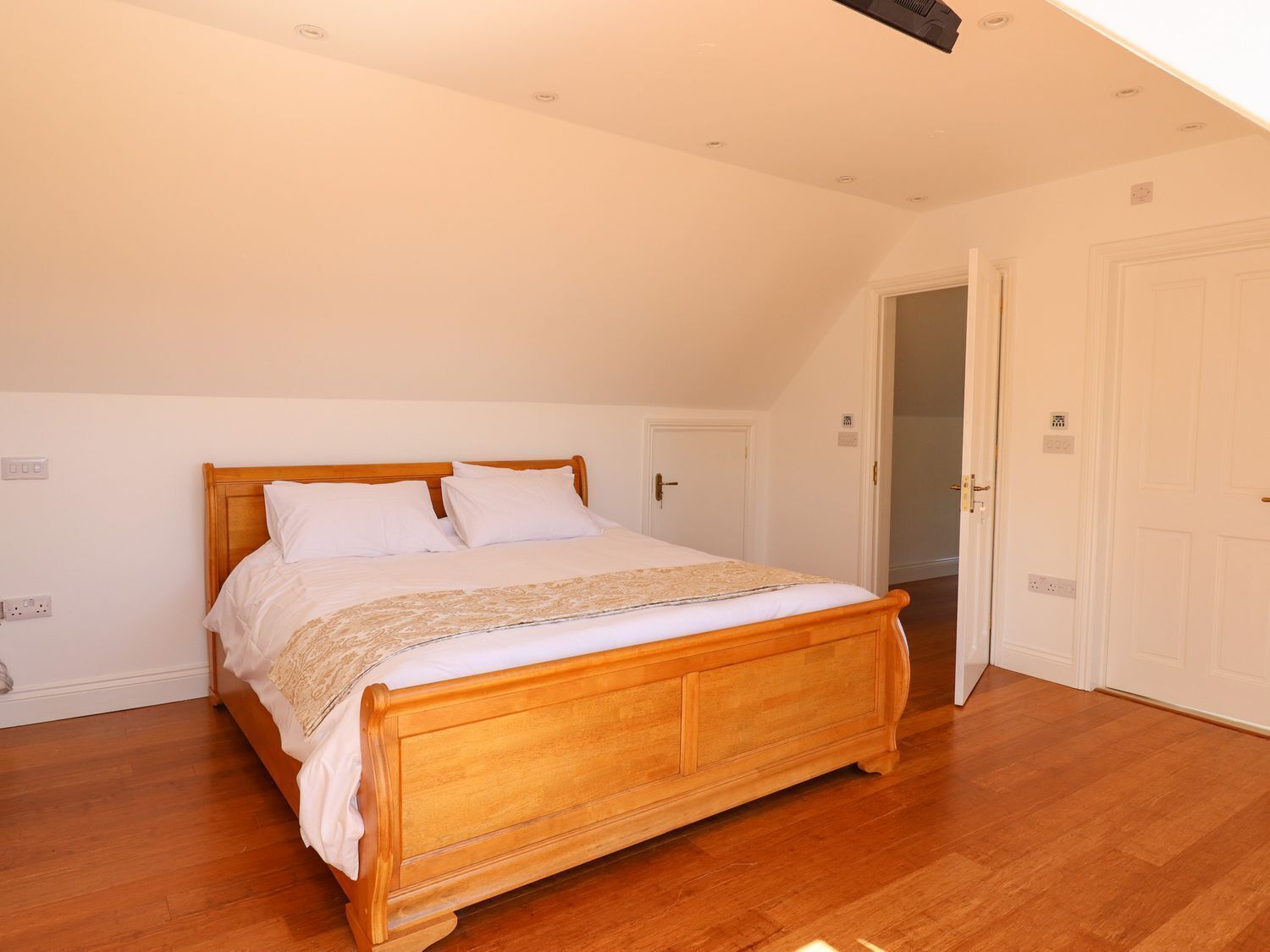 Quarto com cama de madeira, paredes brancas e teto inclinado.