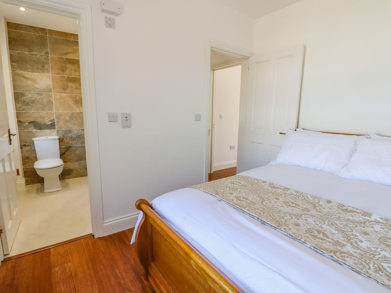 Quarto com cama de madeira, roupa de cama branca e manta estampada.