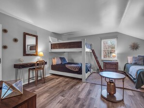 Quarto compacto e moderno com beliche, escrivaninha com cadeira, mesinha e janela com persianas.