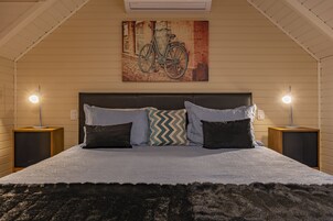 Quarto com cama grande, duas mesas de cabeceira, cabeceira e uma obra de arte na parede com tema de bicicleta.
