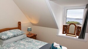 Quarto com cama, mesa de cabeceira, luminária, janela e vista para o mar, além de um espelho.