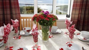 Uma mesa de jantar posta com pratos brancos, guardanapos vermelhos e um vaso de flores.