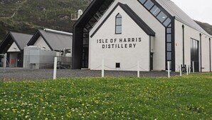 Exterior do edifício da Isle of Harris Distillery, com design arquitetônico moderno, destacando um telhado triangular proeminente e amplas janelas.