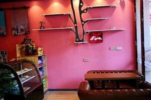 Interior de café com parede rosa, balcão de madeira e área de estar com sofá de couro marrom.