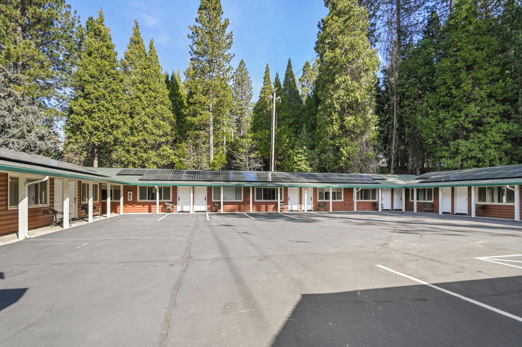 Um motel com uma fileira de quartos, área de estacionamento coberta e um cenário com árvores.