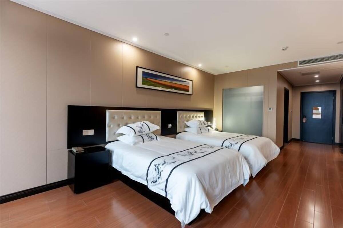 Quarto de hotel com duas camas, um quadro grande na parede e uma porta à direita.
