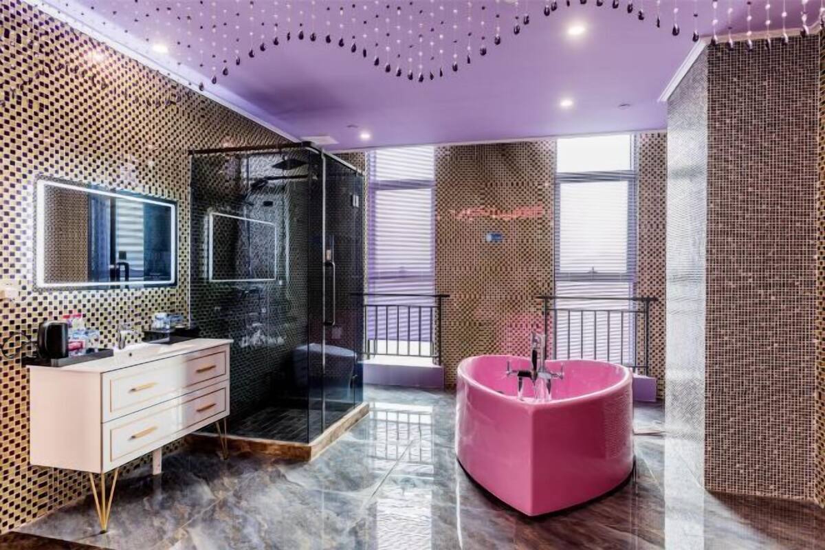 Uma casa de banho moderna com uma banheira rosa, um chuveiro com divisória de vidro e uma toucador com gavetas.