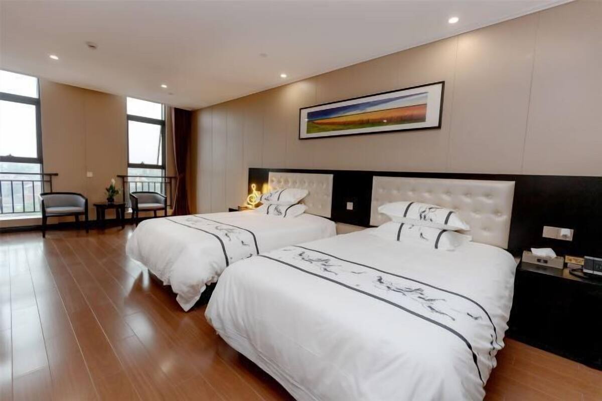 Quarto de hotel com duas camas, uma janela grande, um quadro na parede e uma varanda.