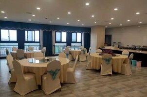 Uma sala de banquetes com mesas redondas e cadeiras, grandes janelas e uma varanda.