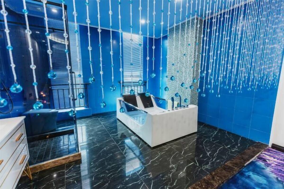 Quarto de hotel moderno com uma receção branca, divisória de vidro e parede azul com decorações suspensas.