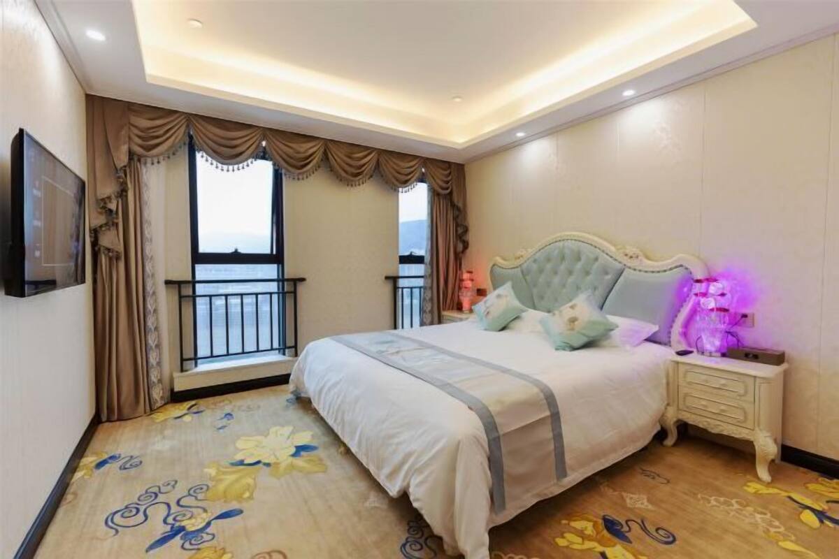 Quarto com cama, mesa de cabeceira e vista para o mar.