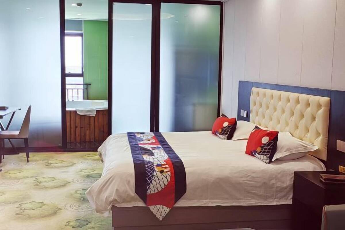 Quarto de hotel com cama, escrivaninha e vista por uma porta de vidro.
