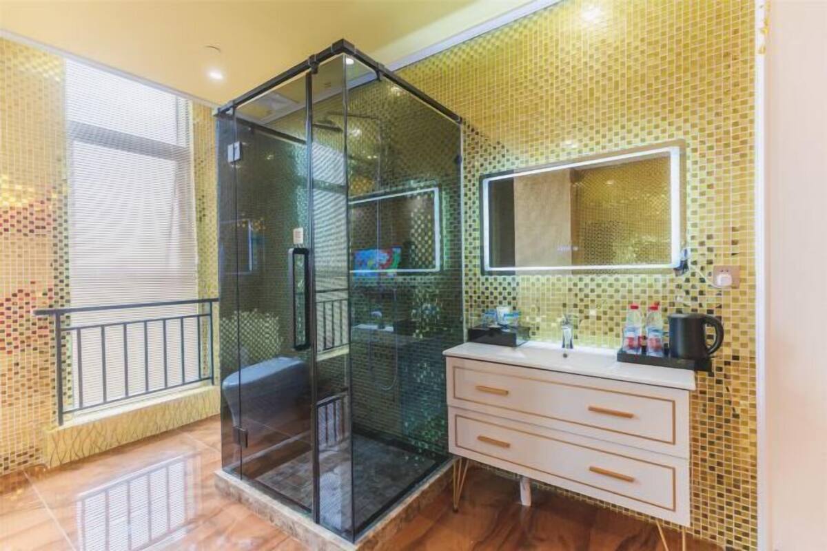 Casa de banho com cabine de duche em vidro, toucador branco com gavetas, espelho e painel de azulejos.