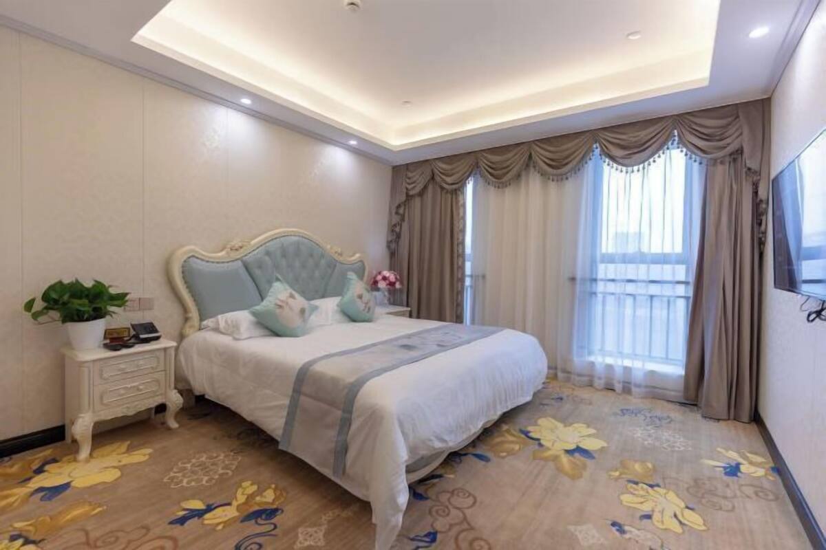 Quarto de hotel com cama, mesa de cabeceira, planta em vaso e vista para o exterior.