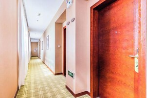 Corredor de hotel com balcão de recepção, porta de madeira e piso coberto por carpete.