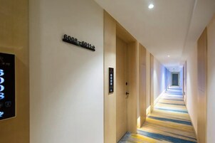 Corredor de hotel com piso carpete, um painel digital e uma porta com placa de número.