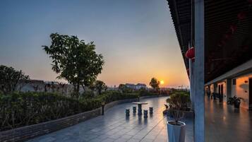 Um terraço ao ar livre com um caminho sinuoso, plantas em vasos e vista para o pôr do sol.