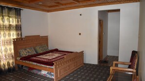 Quarto com cama de madeira, roupa de cama estampada, chão de madeira e mesa de vidro.