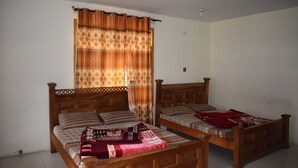 Quarto com duas camas de madeira, cada uma com roupa de cama estampada e cortina com padrão geométrico.