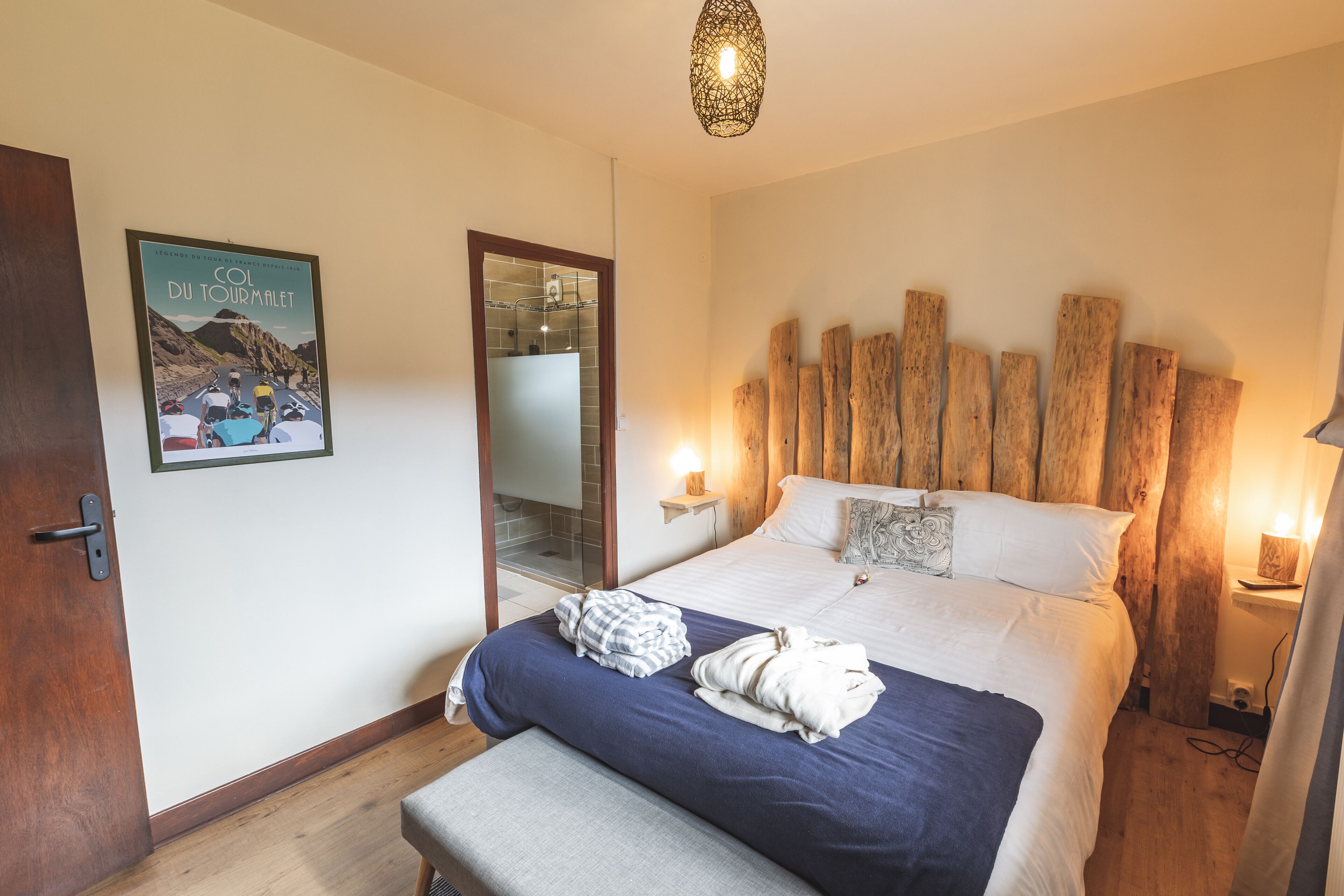 Quarto com cama grande, cabeceira de madeira, luminárias de apoio, um espelho e um cartaz na parede.