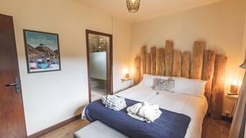 Quarto com cama grande, cabeceira de madeira, luminárias de apoio, um espelho e um cartaz na parede.