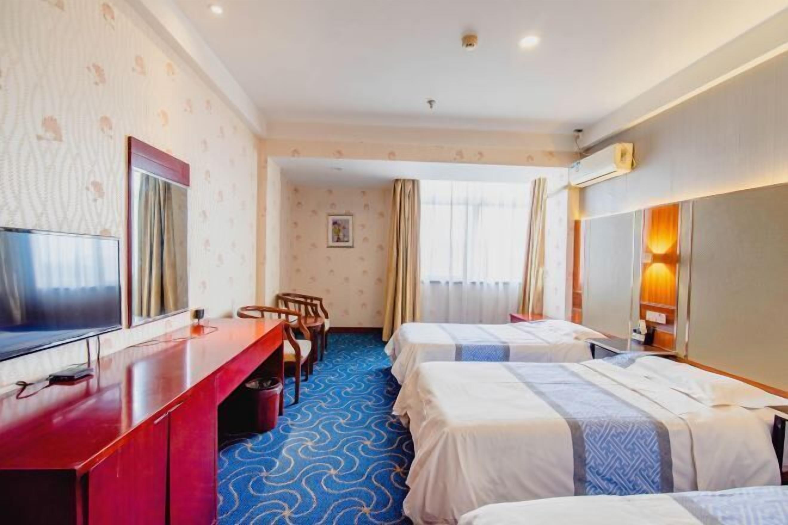 Quarto de hotel com duas camas, uma mesa de trabalho com televisão e uma cadeira.