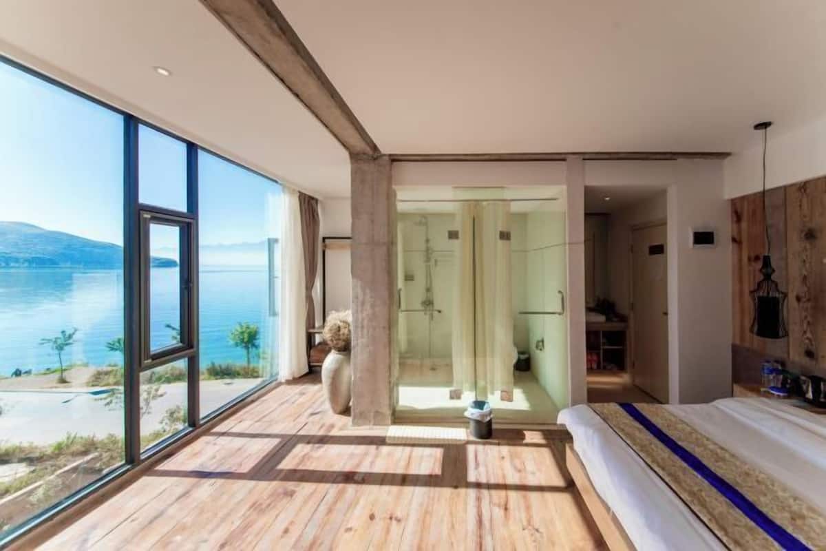 Quarto moderno com grande janela com vista para a água, piso de madeira e cama com faixa azul.