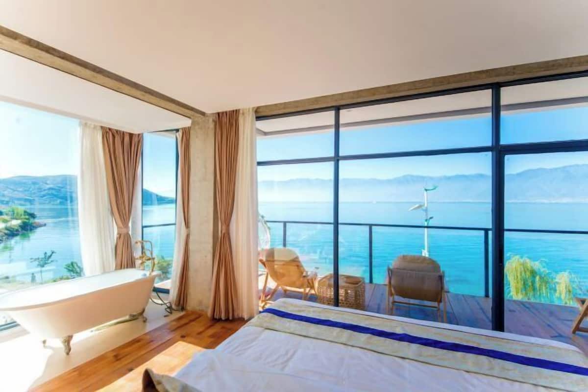 Quarto com cama grande, banheira e vista para o mar.