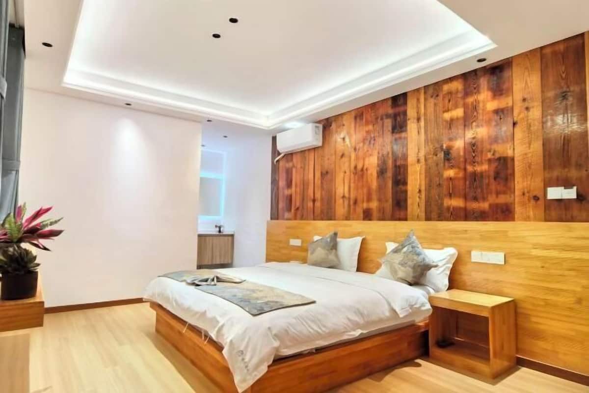 Quarto moderno com cabeceira de madeira, cama com roupa de cama branca, mesa de cabeceira e um vaso com planta.