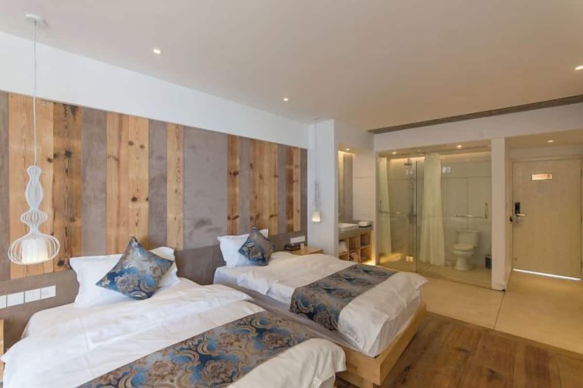 Quarto de hotel moderno com duas camas, cabeceira de madeira e box de vidro.