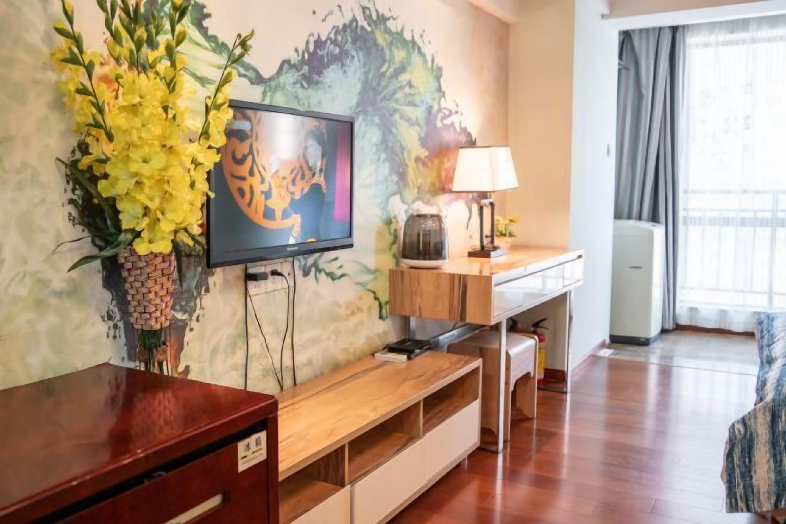 Quarto de hotel com televisão, secretária de madeira e uma janela grande com cortinas.