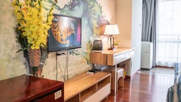 Quarto de hotel com televisão, secretária de madeira e uma janela grande com cortinas.