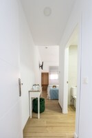 Um corredor estreito com piso de madeira, uma pequena mesa com uma sacola verde e uma toalha azul pendurada na parede.