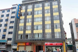 Um hotel com vários andares, fachada em amarelo e cinza, algumas lojas no térreo e uma entrada visível.