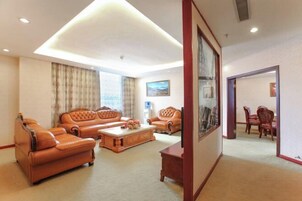 Quarto de hotel com sofá, mesa de centro, uma pintura e área de refeições com cadeiras e mesa.