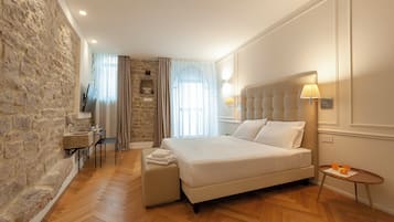 Quarto de hotel com parede de destaque em pedra, cama com roupa de cama branca, mesa pequena com abajur e vista para o exterior.