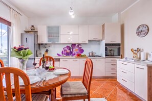 Cozinha moderna com armários brancos, mesa de jantar posta com pratos, copos e um vaso de flores.