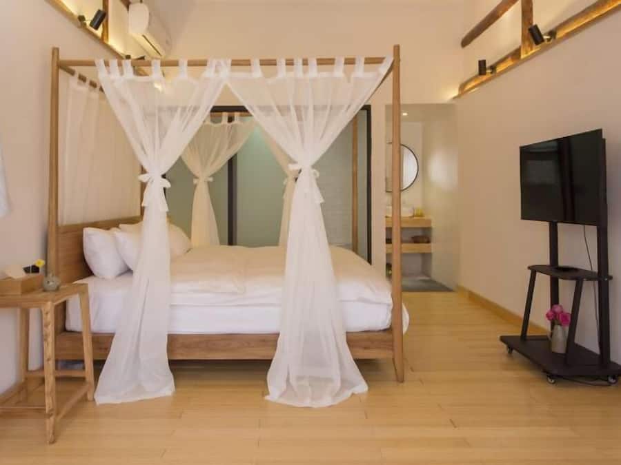 Quarto com cama de madeira, dossel branco, mesa de cabeceira, suporte para TV e espelho.